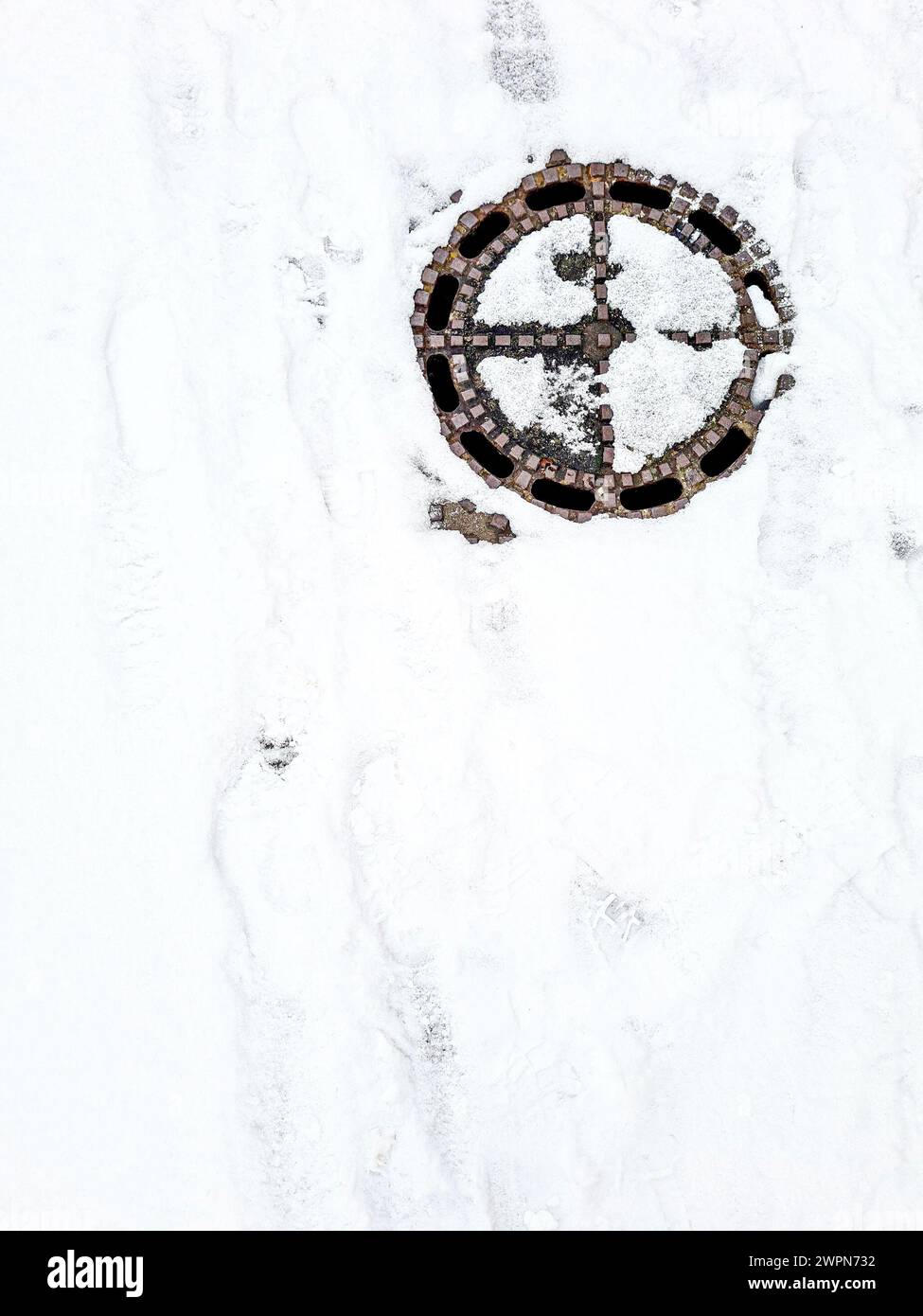 Tracks and patterns in the snow and the manhole cover covered in snow ...