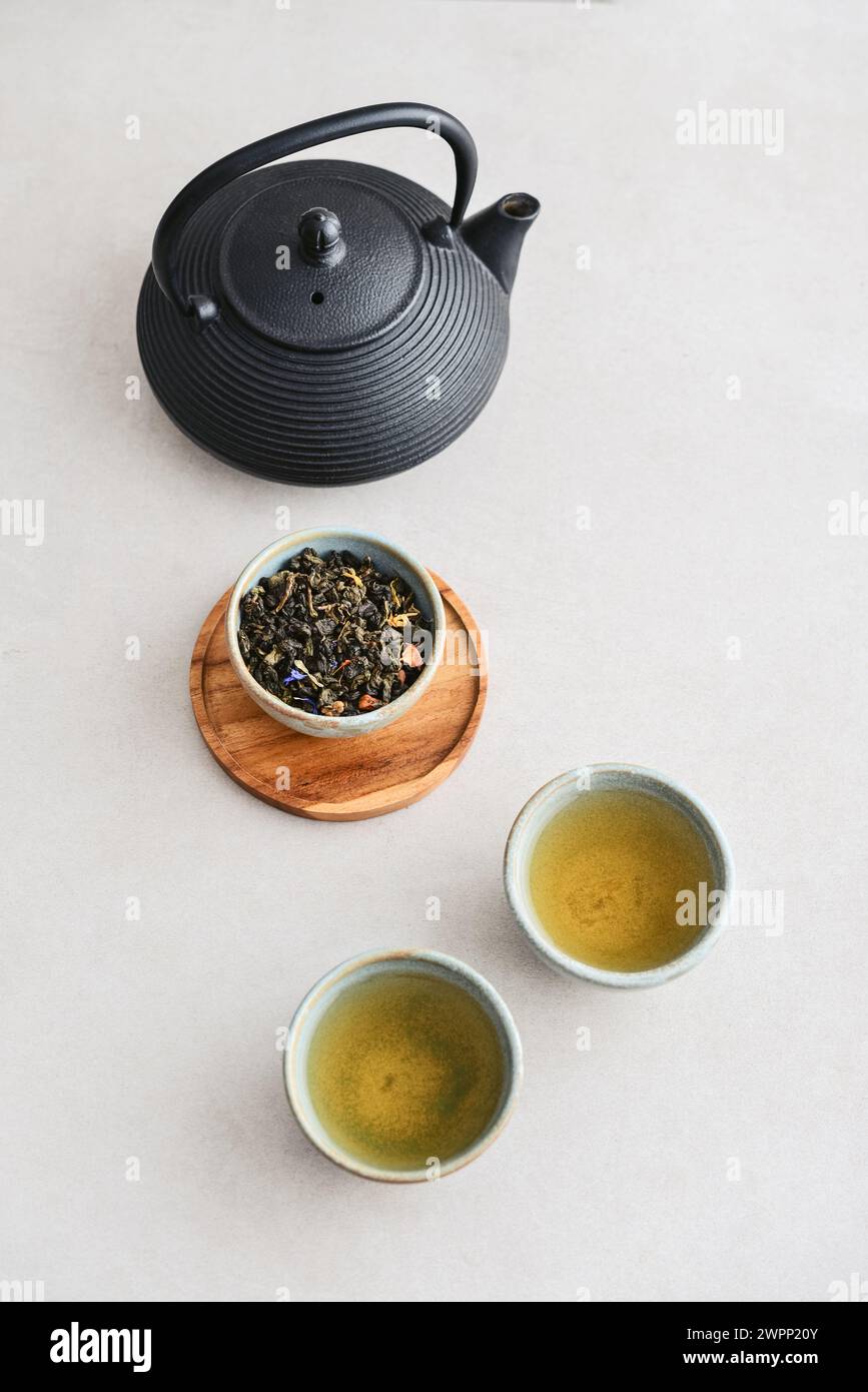 Black cast iron teapot and two ceramic cups of green tea on a light ...