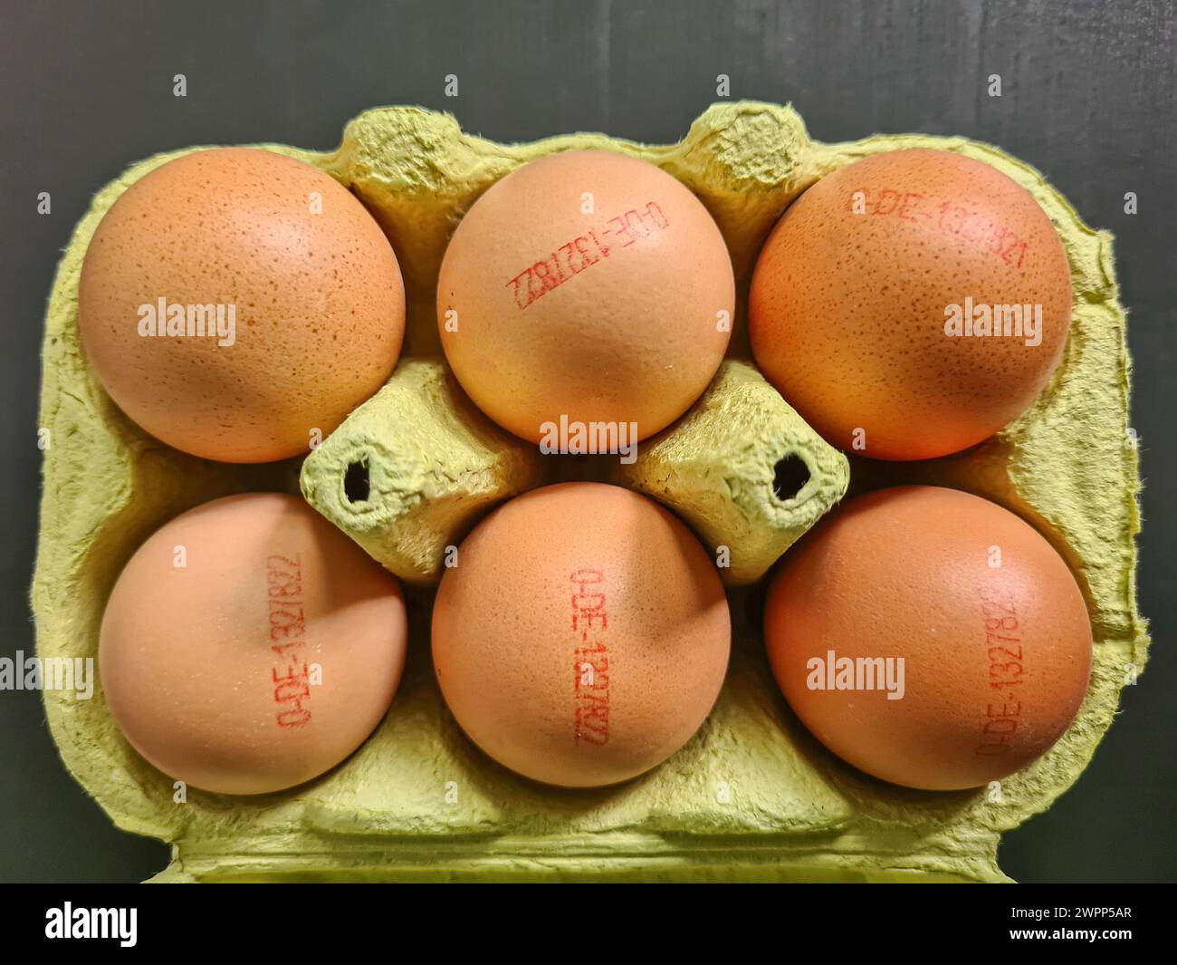 Six brown eggs with stamp of origin in a green egg carton on a dark ...