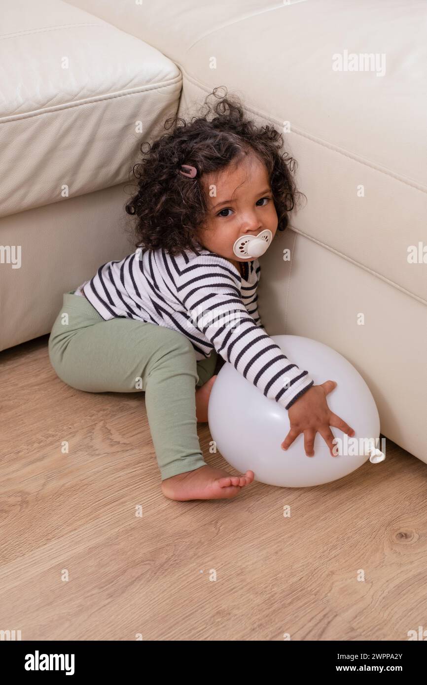 An upset or sad toddler with a pacifier, clutching a white balloon ...