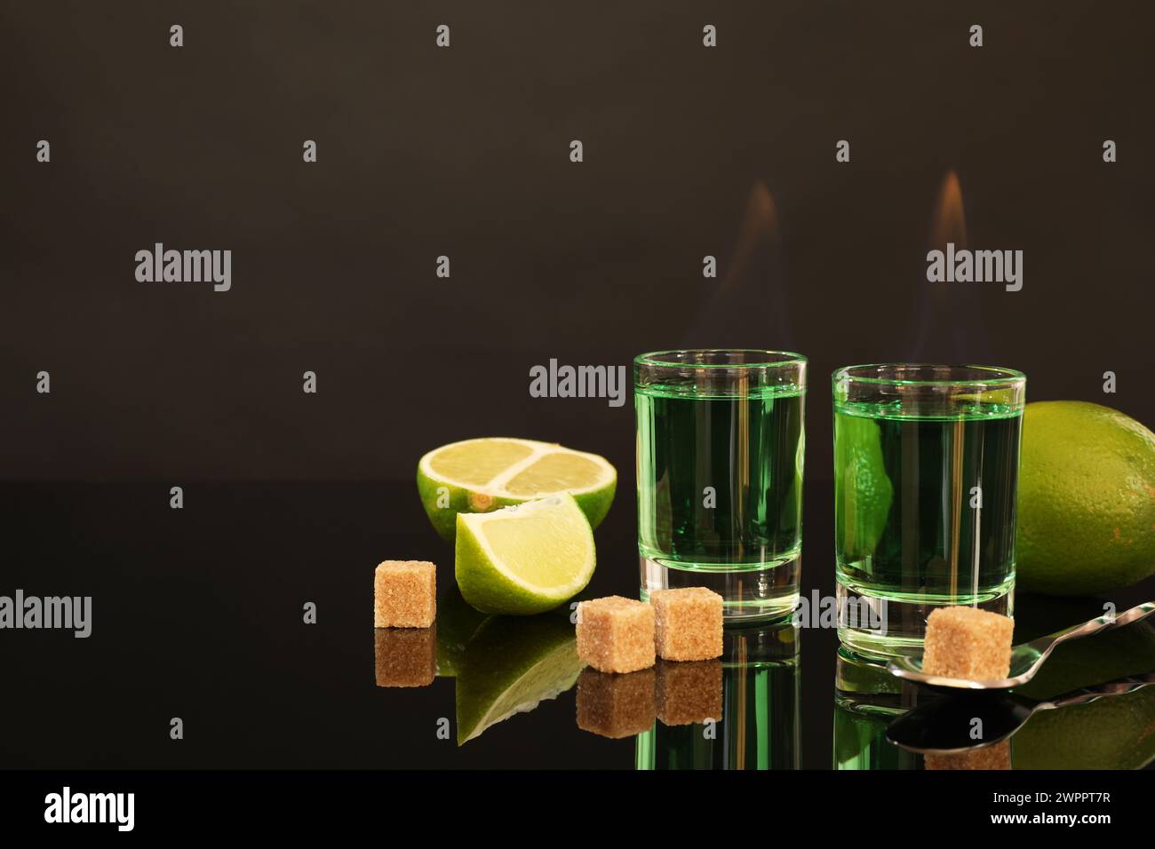 Flaming absinthe in shot glasses, brown sugar, lime and spoon on mirror ...