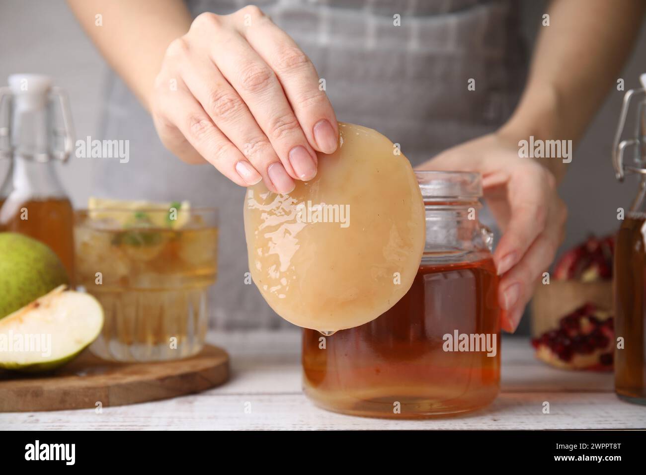 Woman putting Scoby fungus into jar with kombucha at white wooden table ...