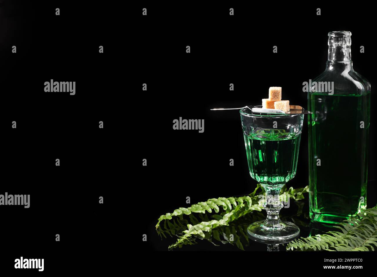Absinthe, brown sugar, spoon and green leaves on mirror table, space ...