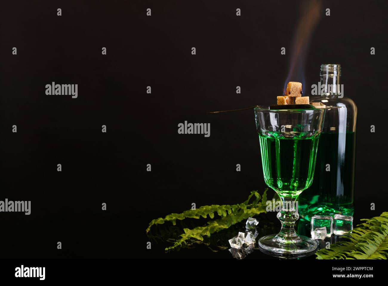 Absinthe, flaming brown sugar, ice cubes and green leaves on mirror ...