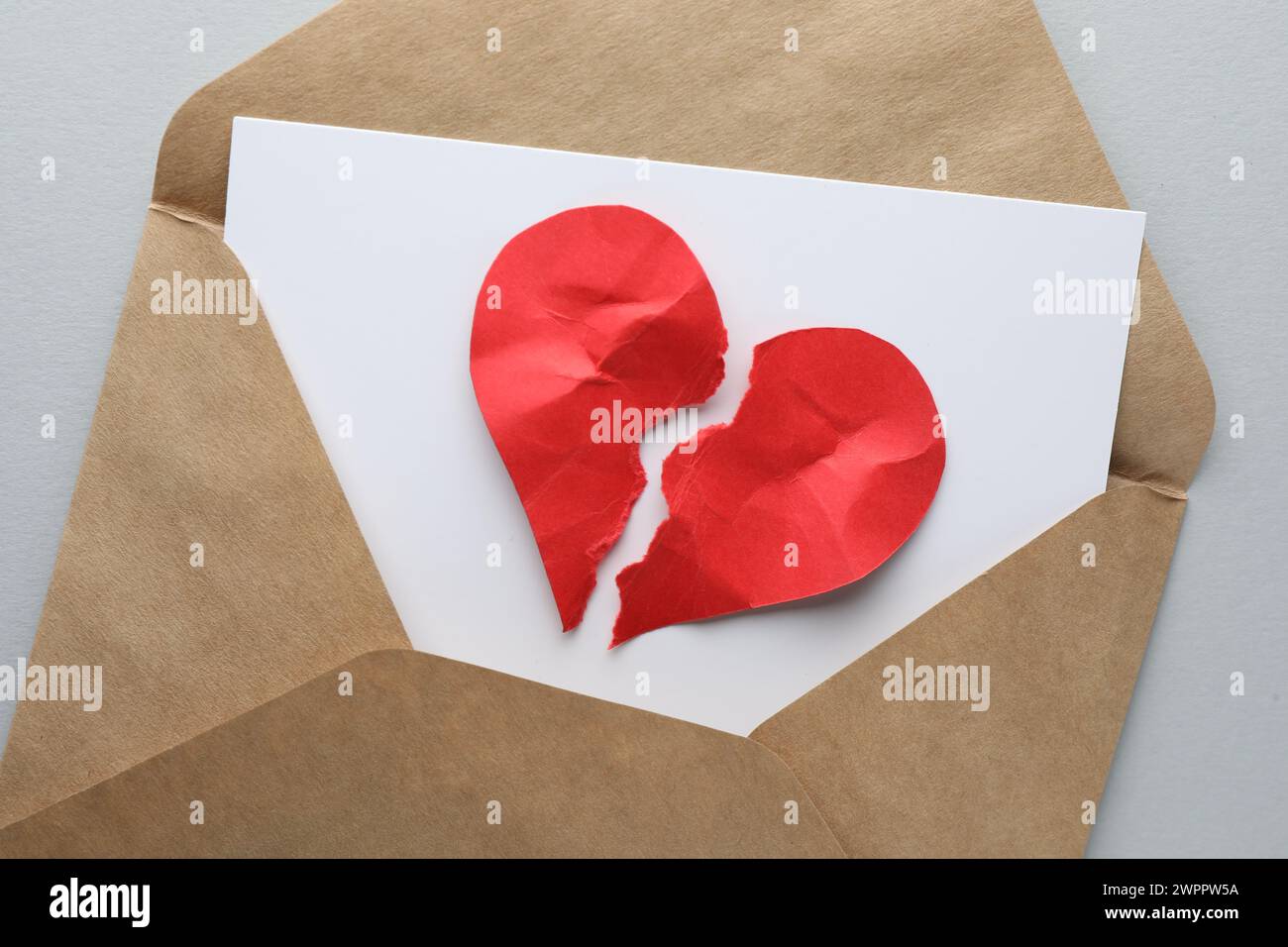 Envelope with halves of torn red paper heart on white background, top ...