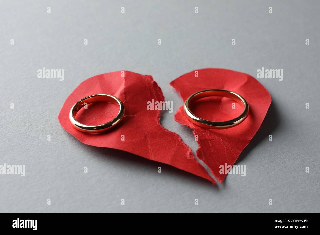 Halves of torn red paper heart and wedding rings on white background ...