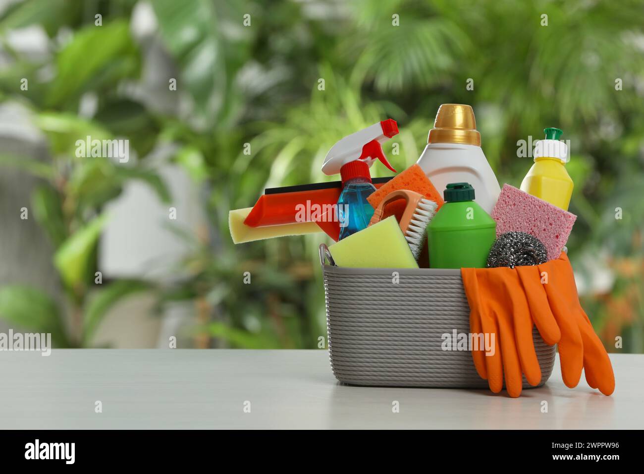 Different cleaning products in basket on light grey table indoors ...