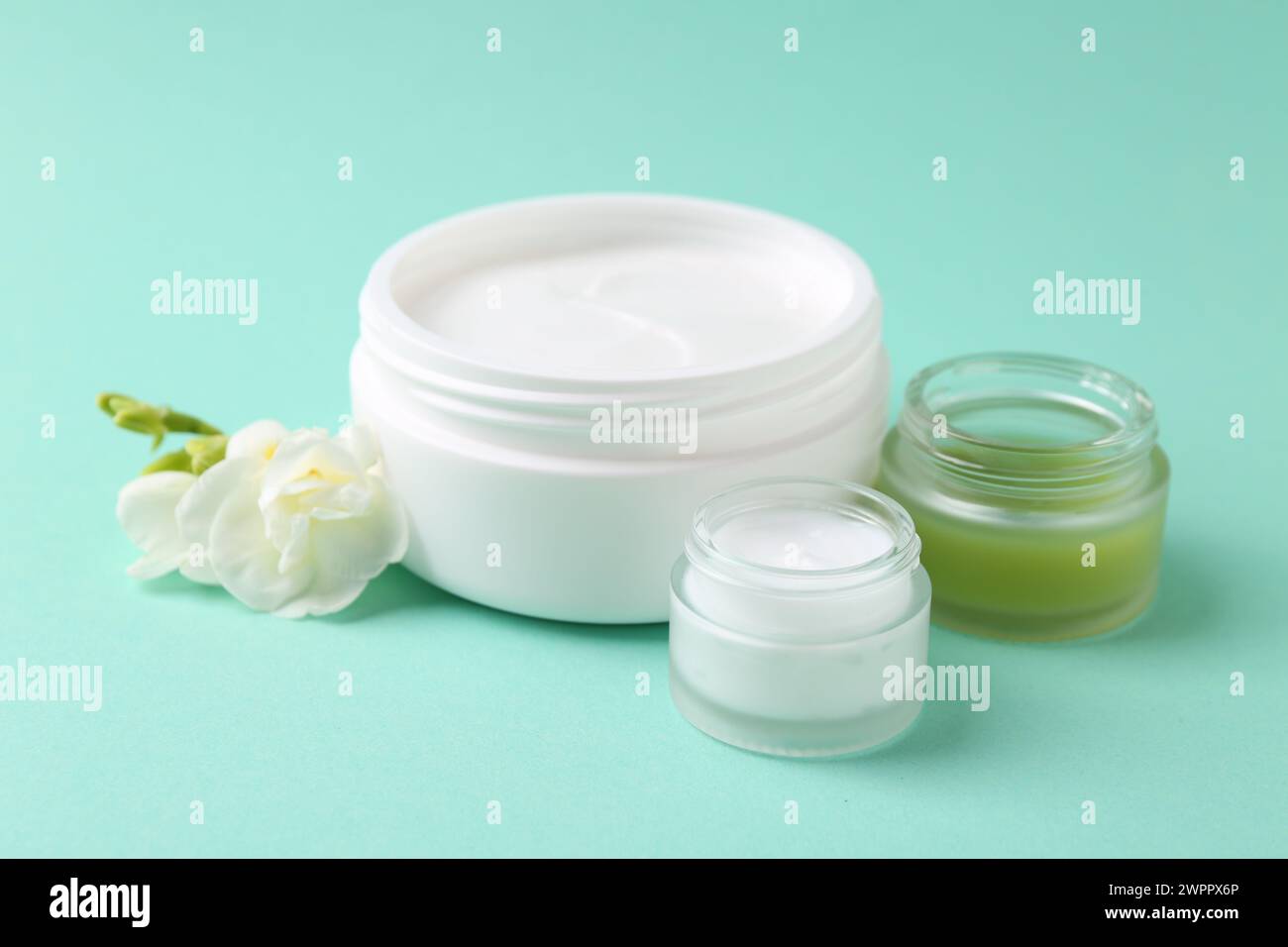 Moisturizing cream in open jars and freesia flower on turquoise ...
