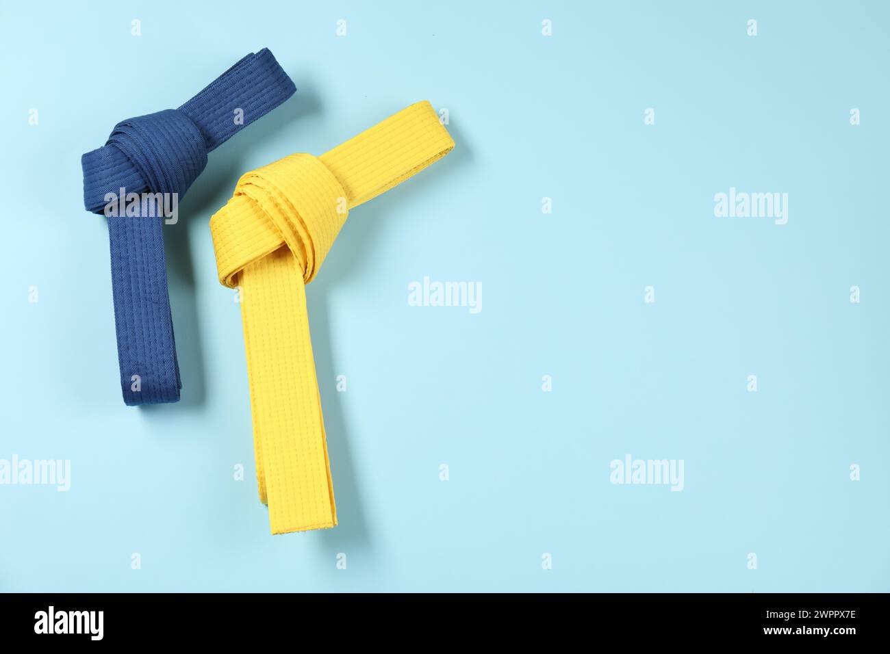 Colorful karate belts on light blue background, flat lay. Space for ...