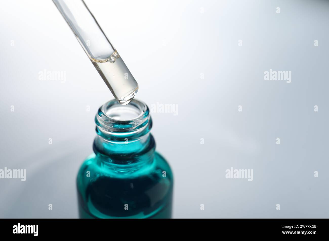 Dripping moisturizing serum from pipette into bottle on light grey ...