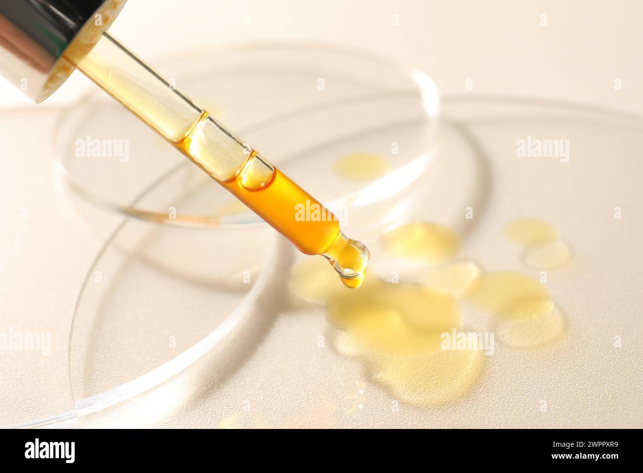 Dripping moisturizing serum from pipette on beige background, closeup ...