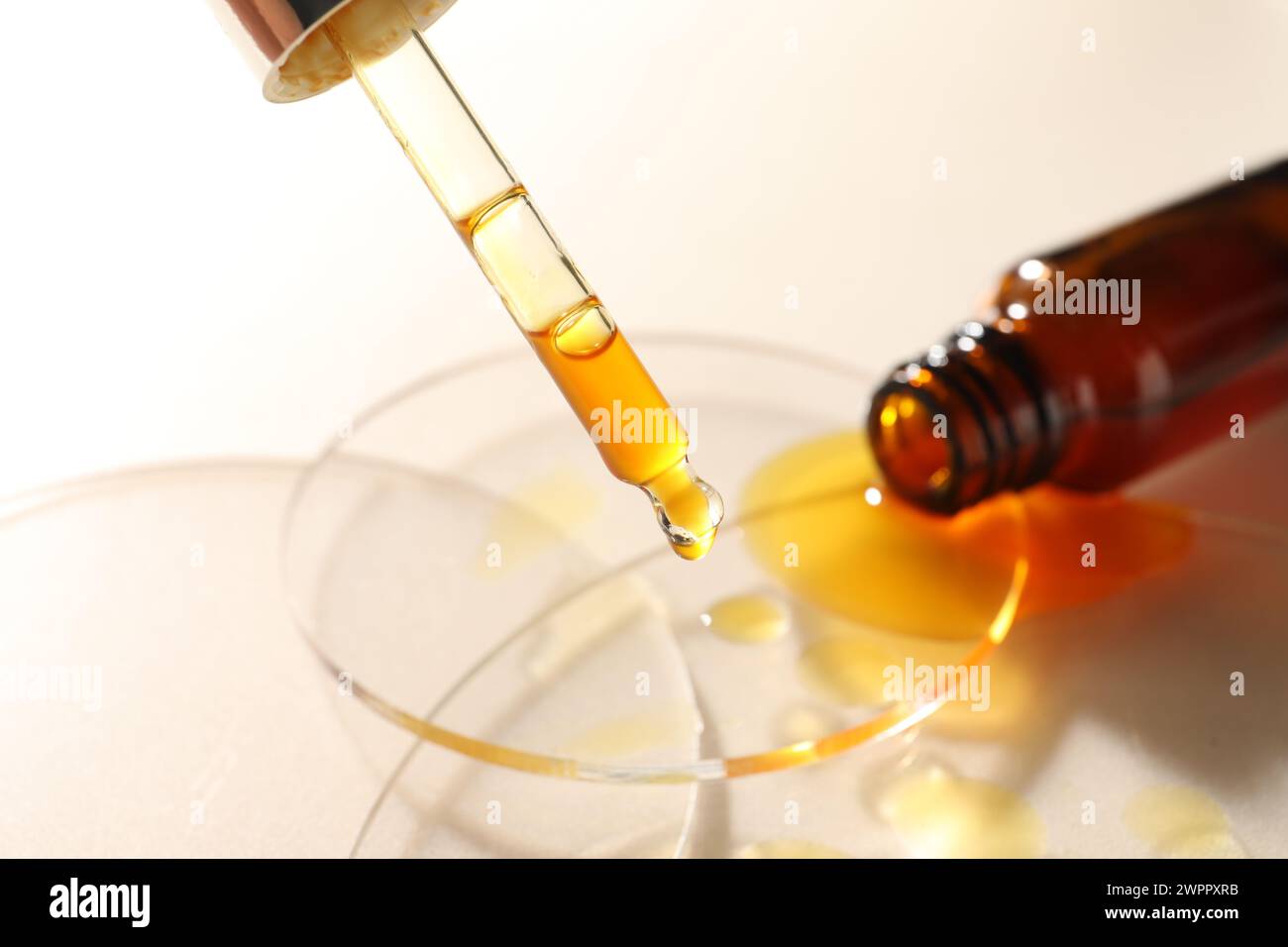 Dripping moisturizing serum from pipette on beige background, closeup ...