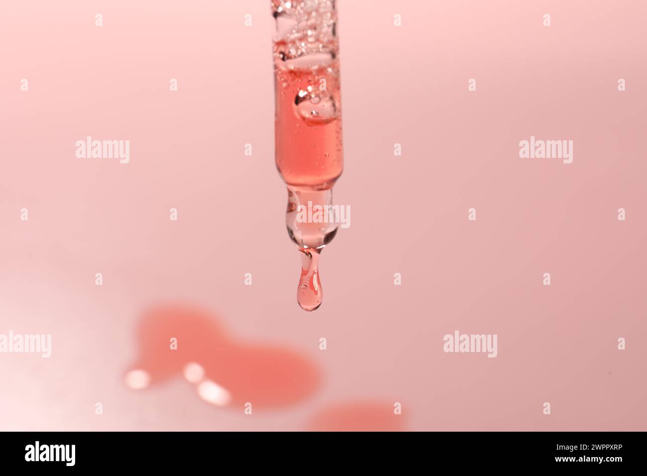 Dripping moisturizing serum from pipette on pink background, closeup ...