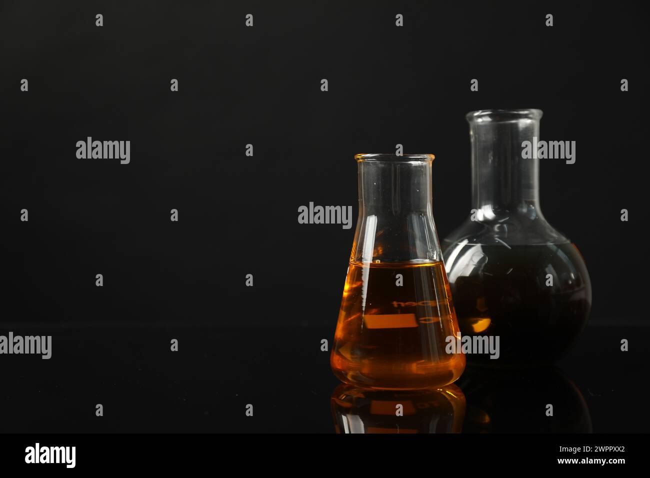 Glass flasks with different types of oil on black background, space for ...