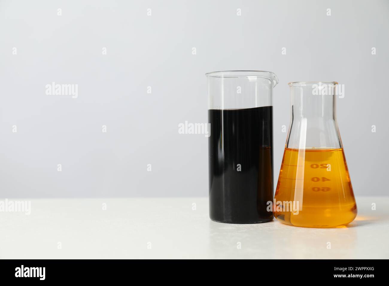 Beaker and flask with different types of oil on white table, space for ...