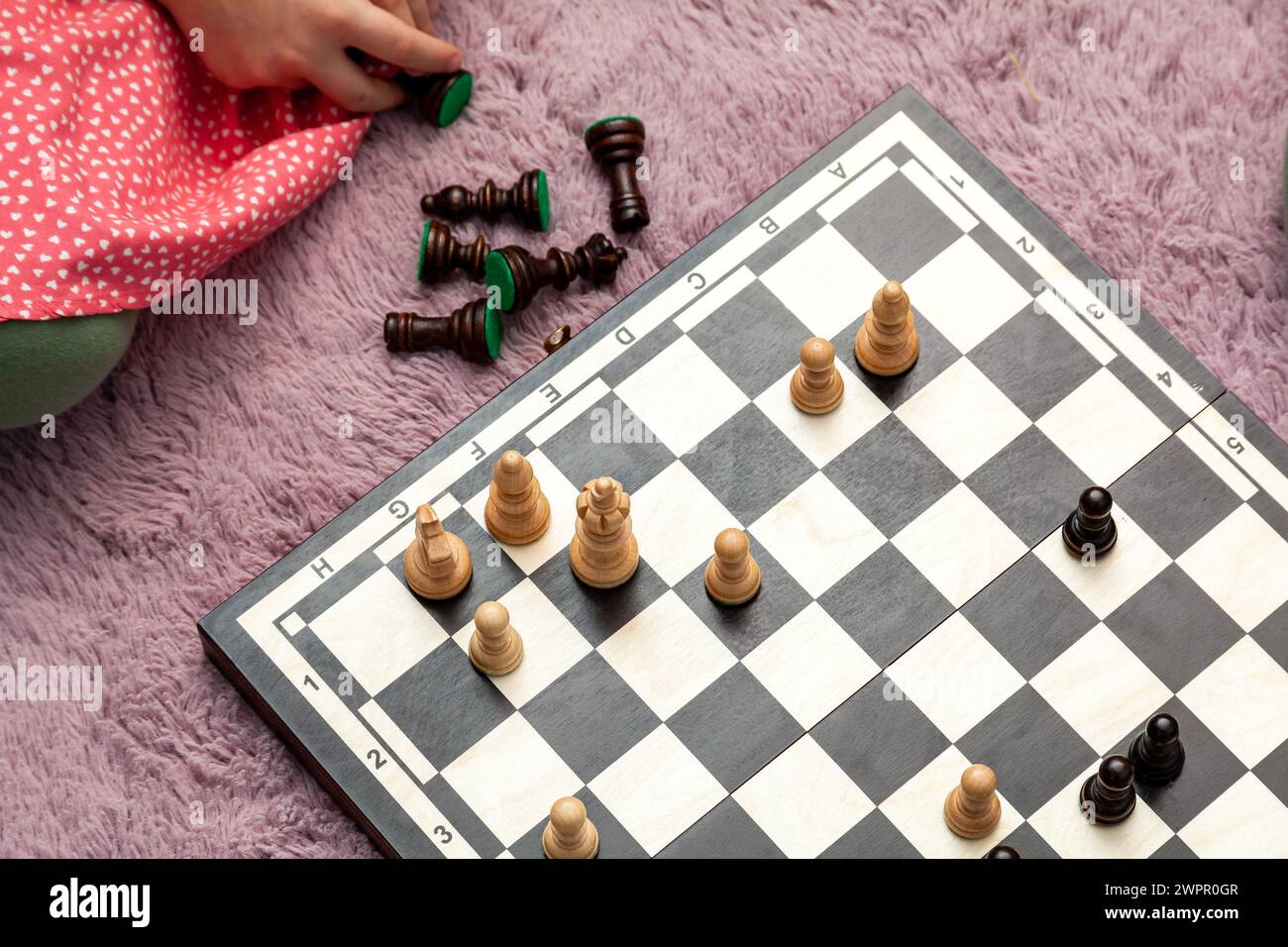 Young child playing chess pieces laid out on the ground, soft purple ...