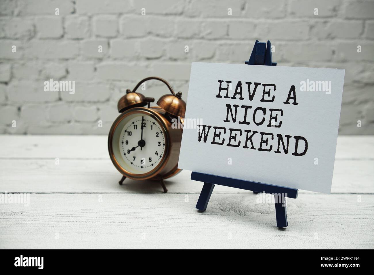 Have a Nice Weekend text and alarm clock on white brick wall and wooden ...