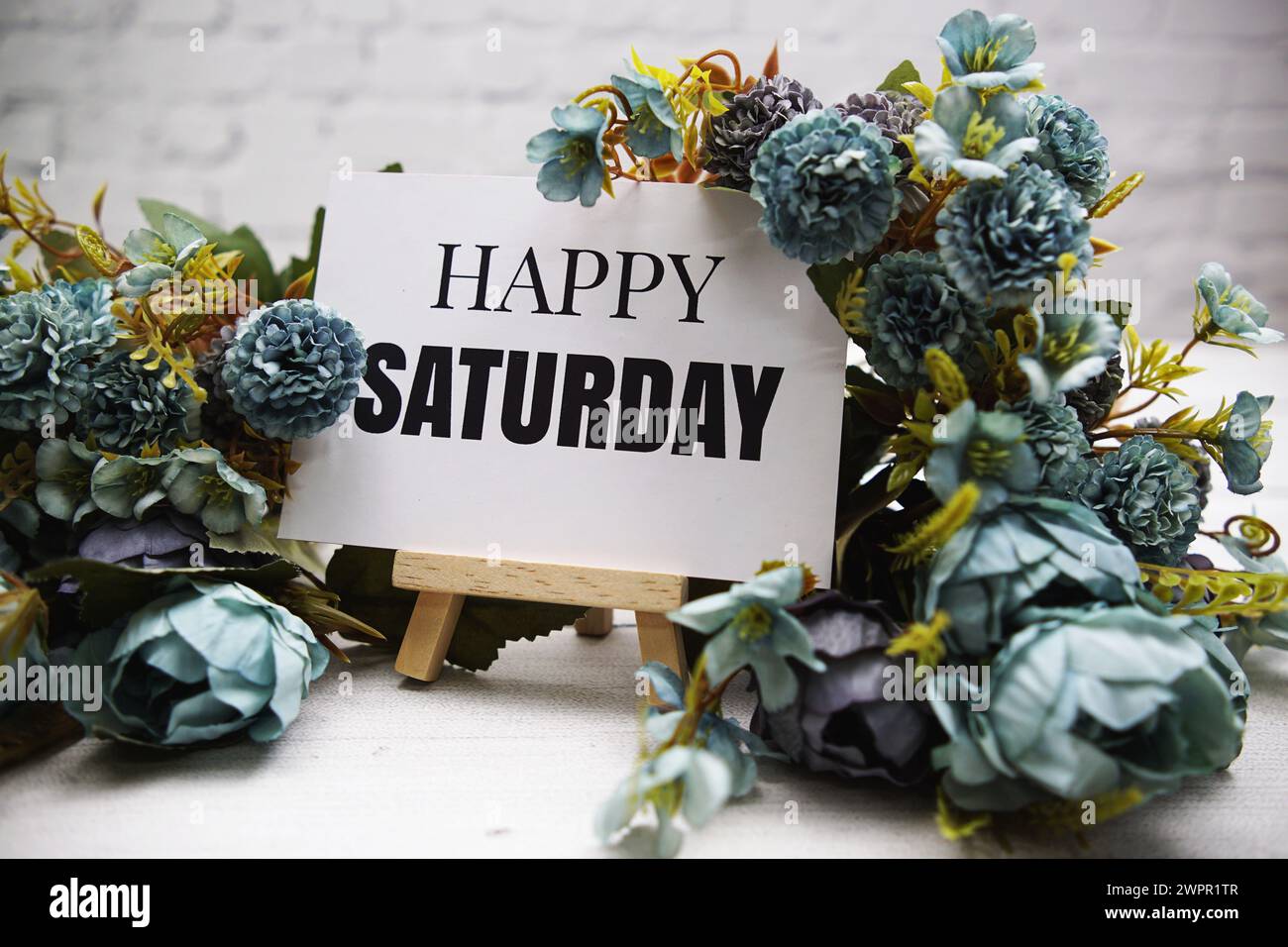 Happy Saturday text on wooden easel standing on white brick wall and ...