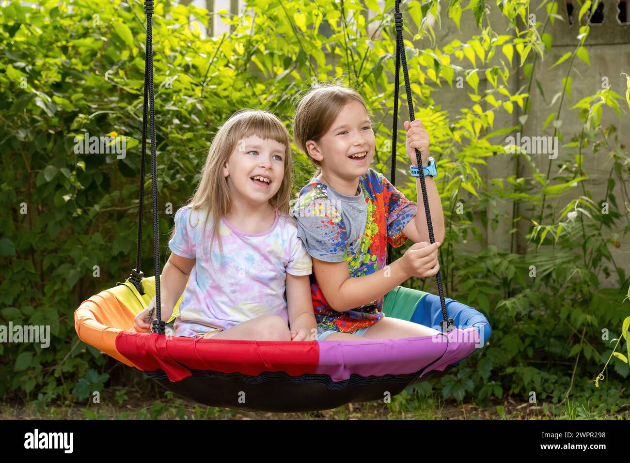 Two young girls, children sitting side by side on a round swing, joyful ...