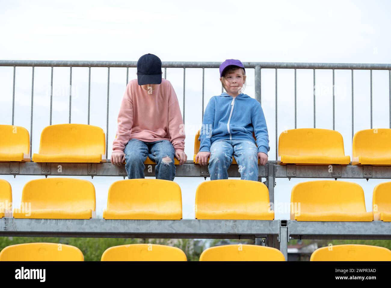 Two young girls, children sitting on stadium seats, bleachers, chairs ...