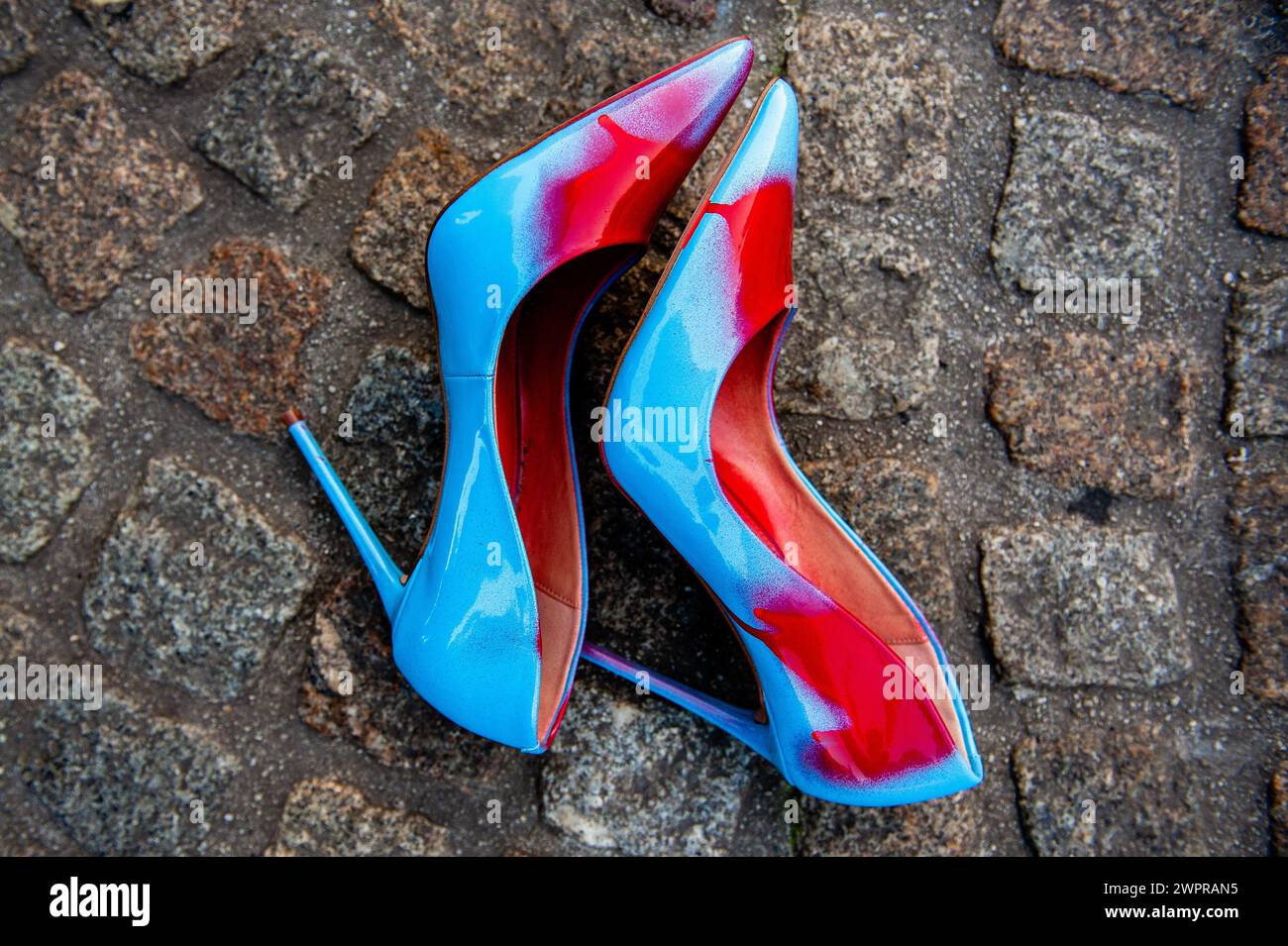A pair of high heels are seen placed on the ground with red paint in ...
