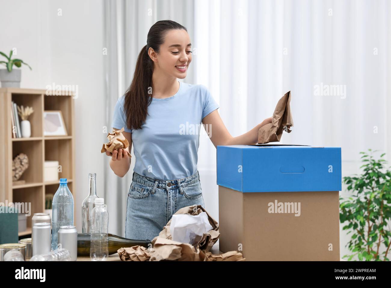 Garbage sorting. Smiling woman throwing crumpled paper into cardboard ...