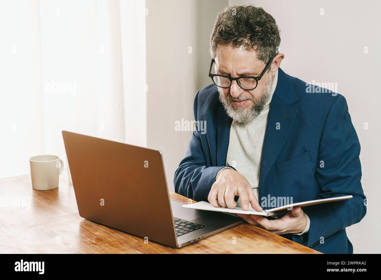 Business casual man reading a notebook by laptop - Concentrated on ...