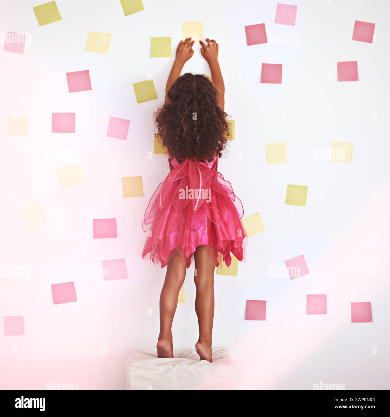 Kid, girl and play with sticky notes in against wall, standing on ...