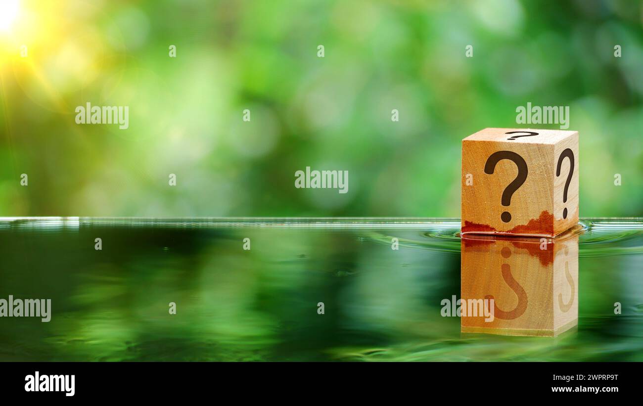 Wooden cube block with engraved question mark symbol on water with ...