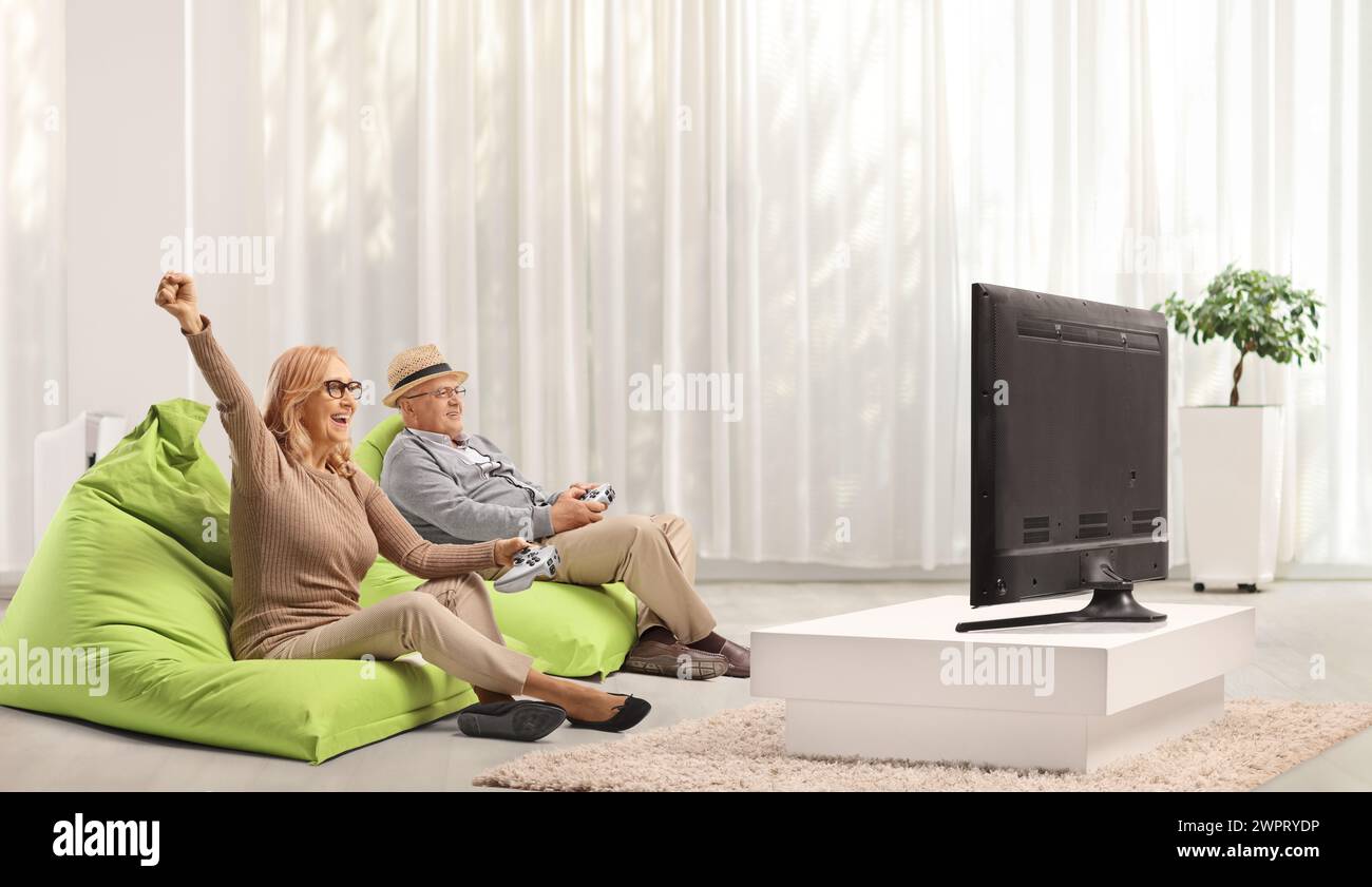 Happy mature woman and an elderly man playing video games at home in ...