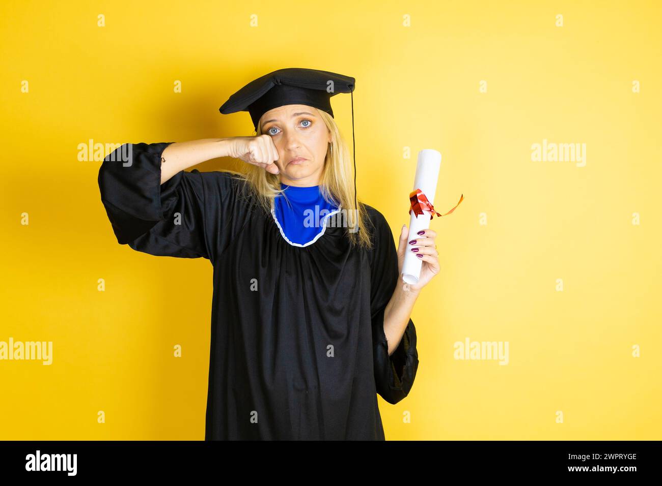 Beautiful blonde young woman wearing graduation cap and ceremony robe ...