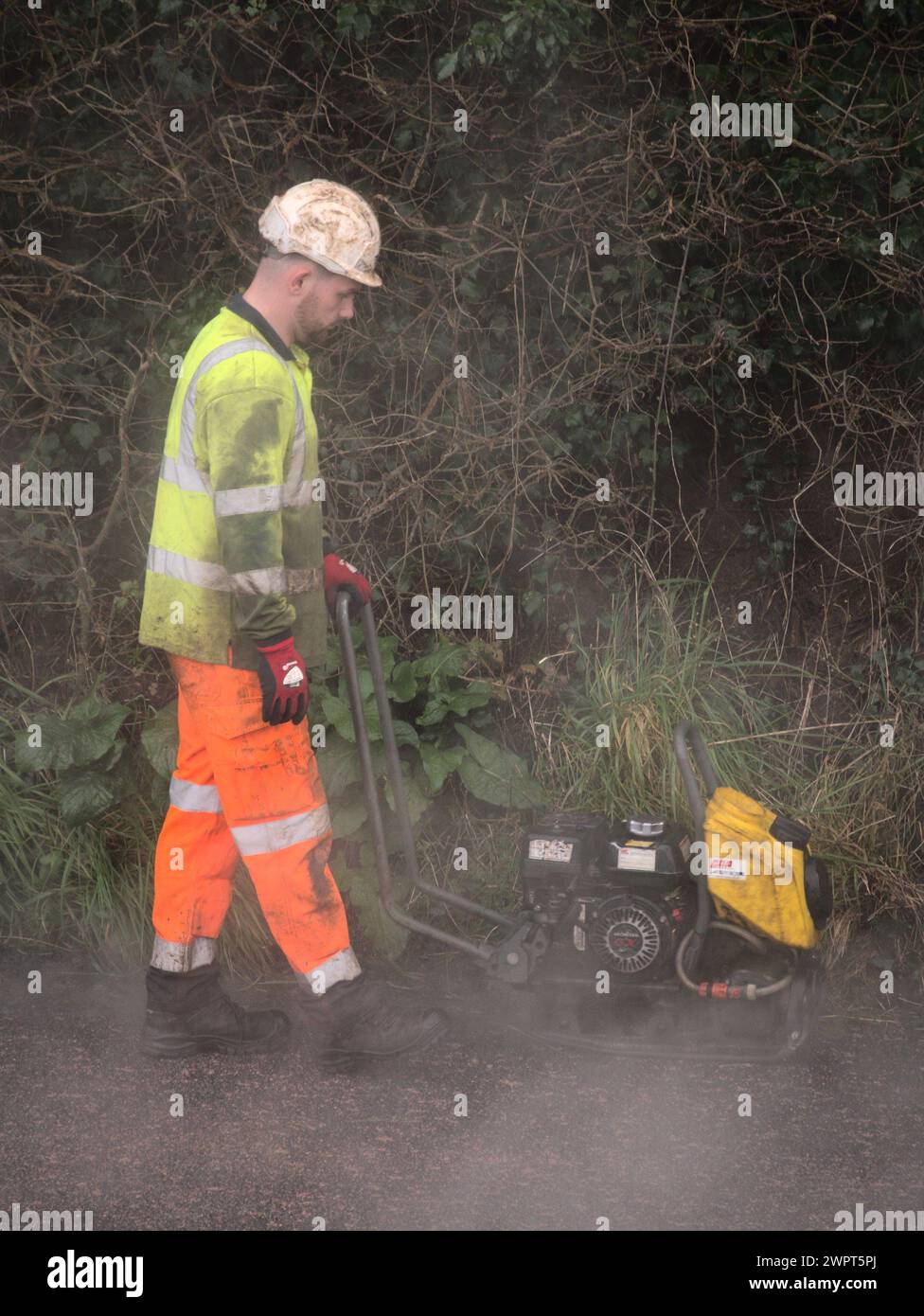 Worker using a vibrating plate compactor during Road resurfacing work ...