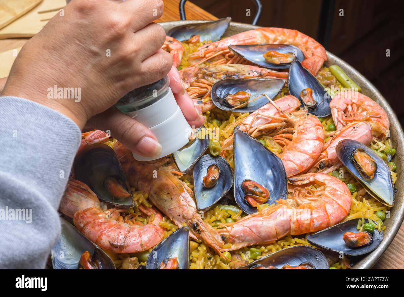 Close-up of a hand seasoning traditional seafood paella with rich ...