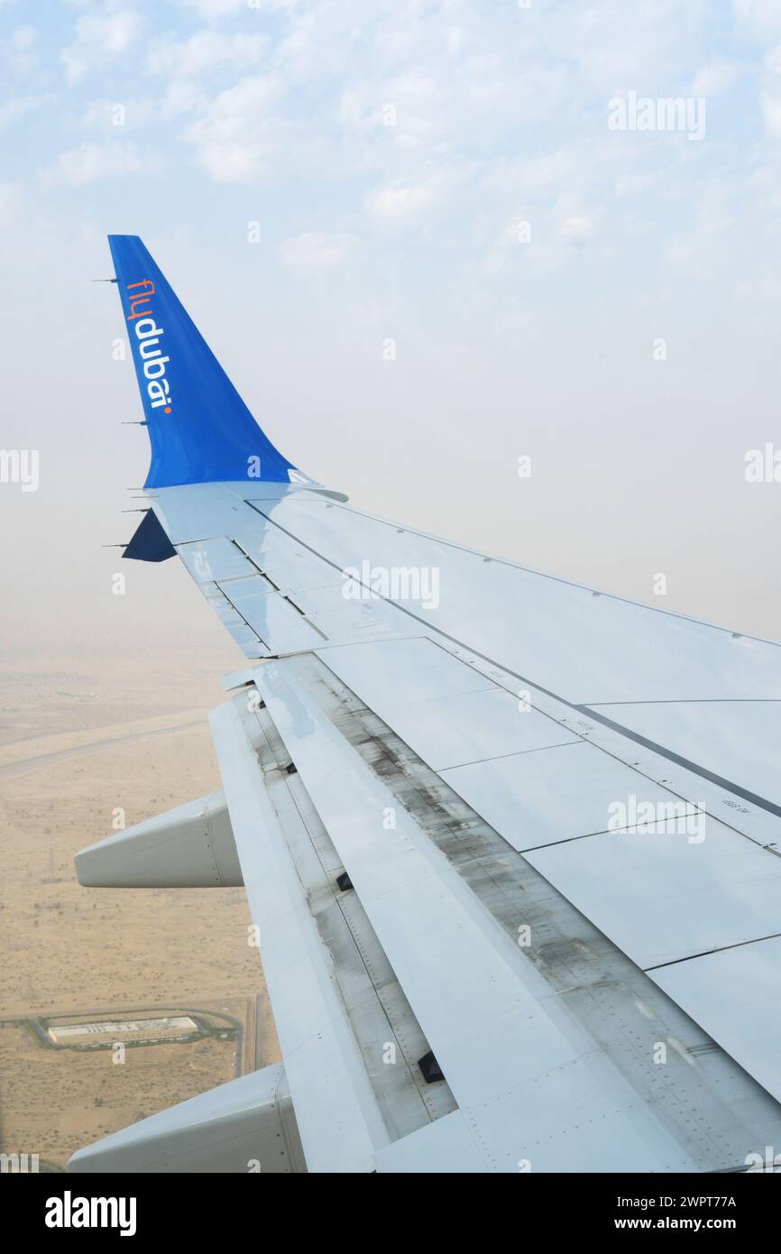 The wing of a Flydubai aircraft against a cloudy sky above the desert ...