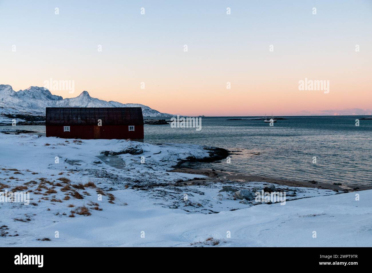 A traditional norwegian red barn enclosed by rugged mountains and snow ...