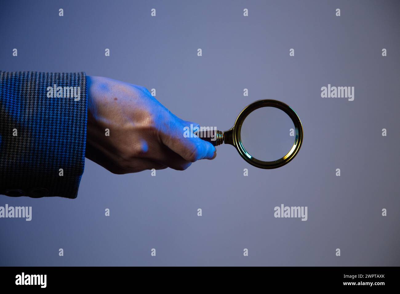Right female hand with a magnifying glass on a gray background. Blue ...