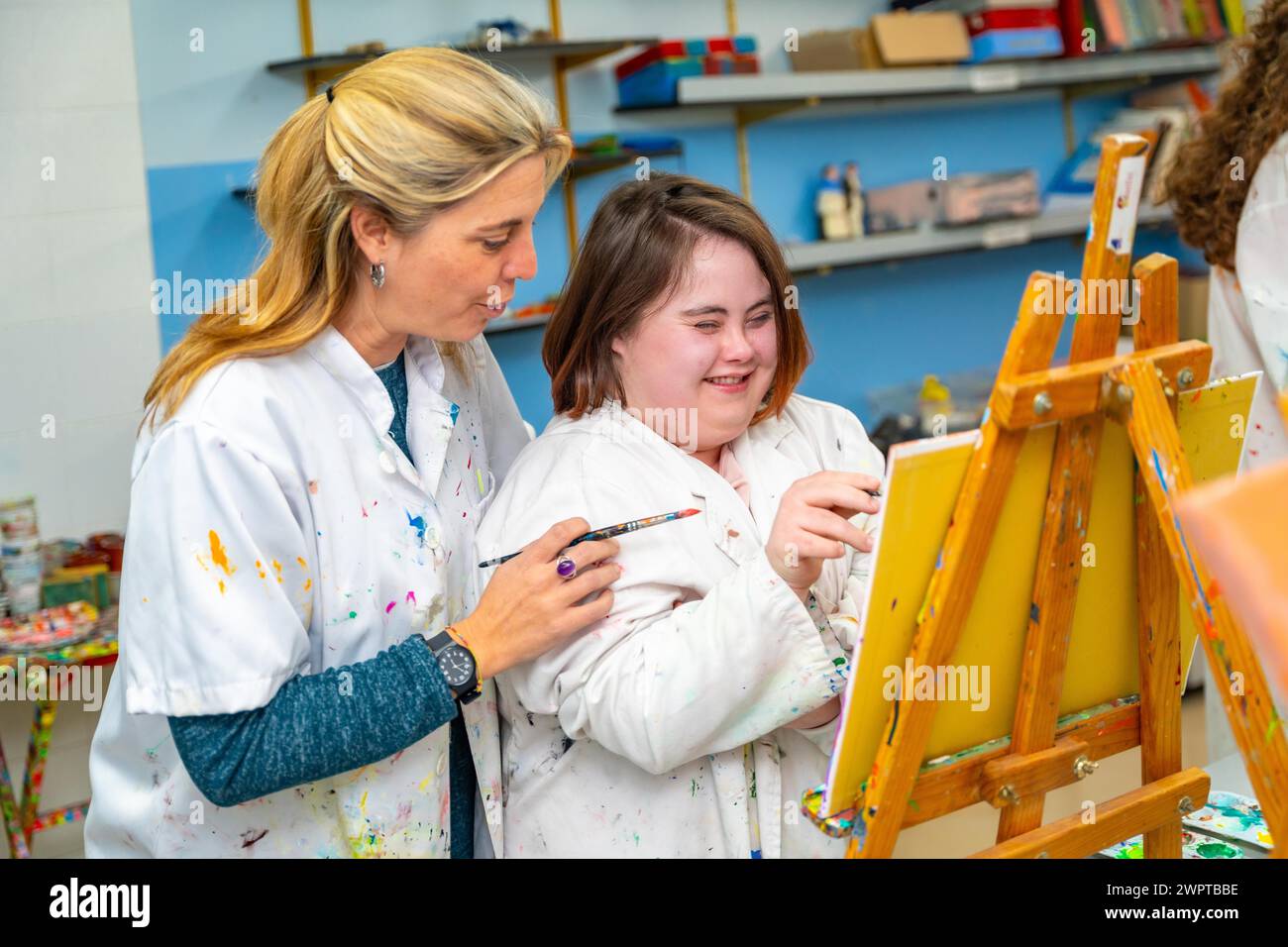 Adult caucasian teacher helping a smiling woman with down syndrome ...
