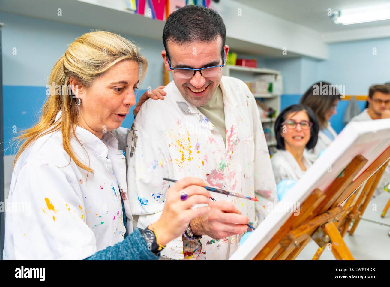 Instructor helping a disabled man during painting class in a center for ...