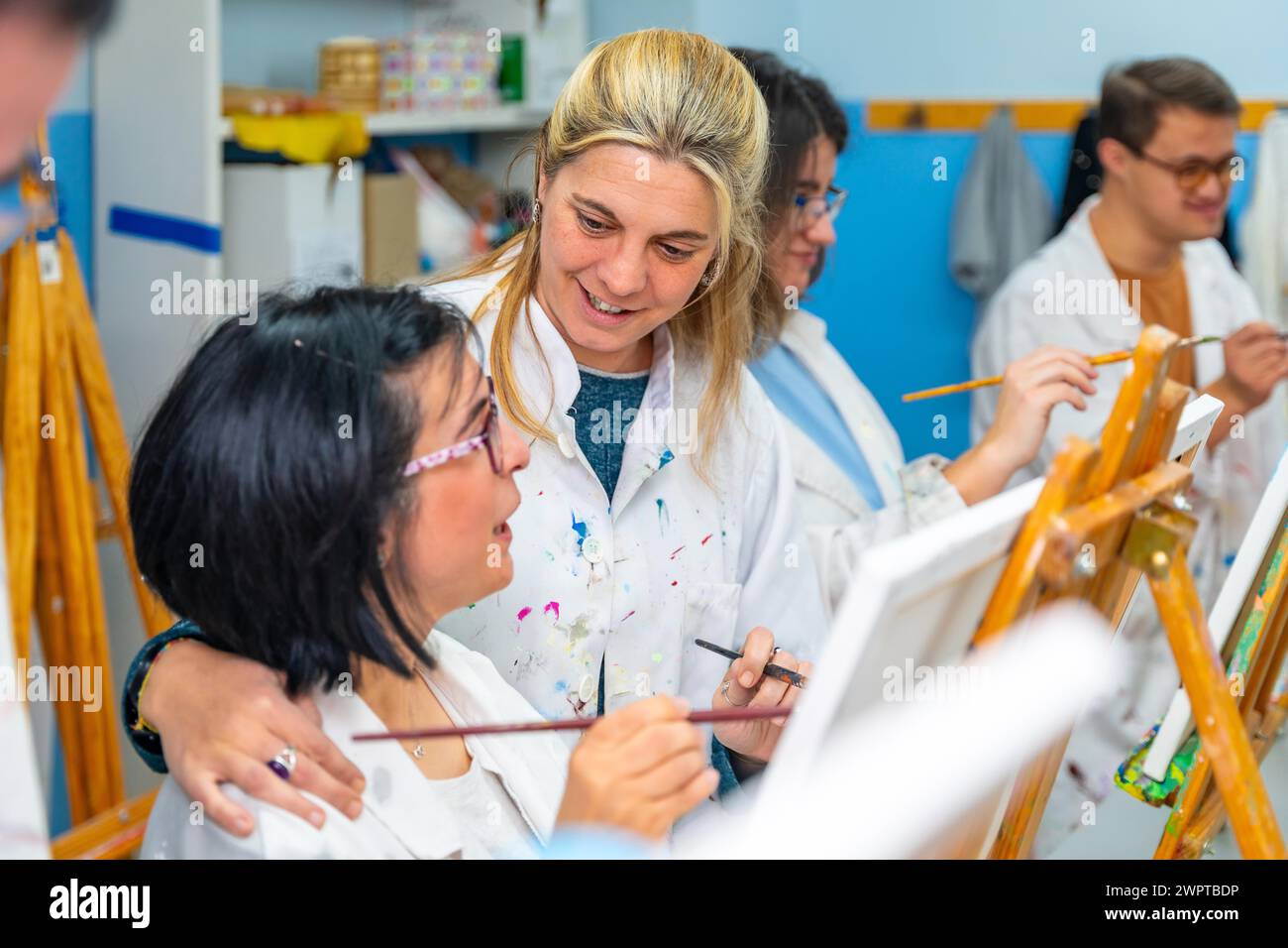 Teacher encouraging a disabled woman during painting class with other ...