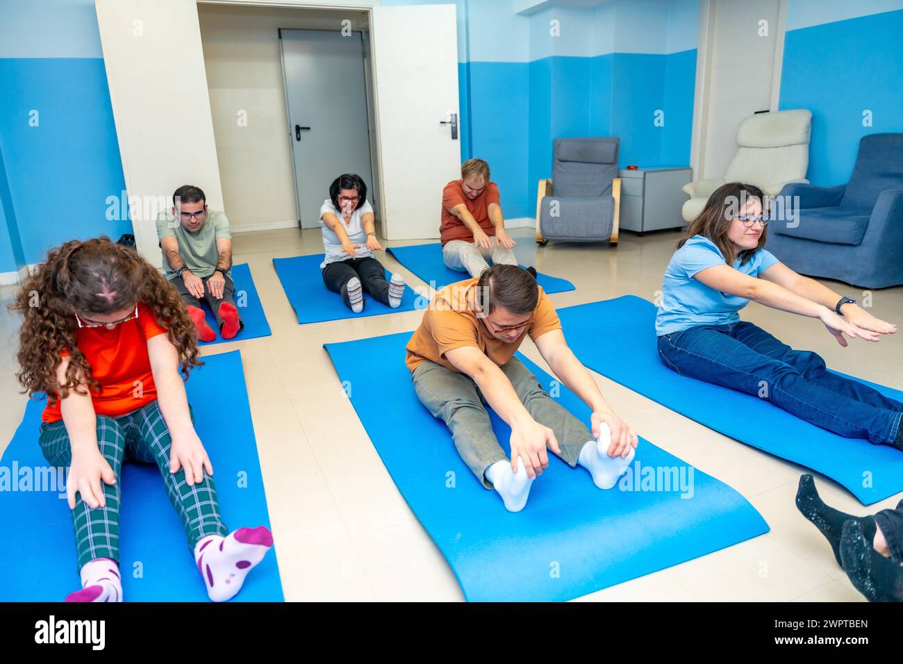 Group of adult intellectual disabled people stretching sitting on a mat ...