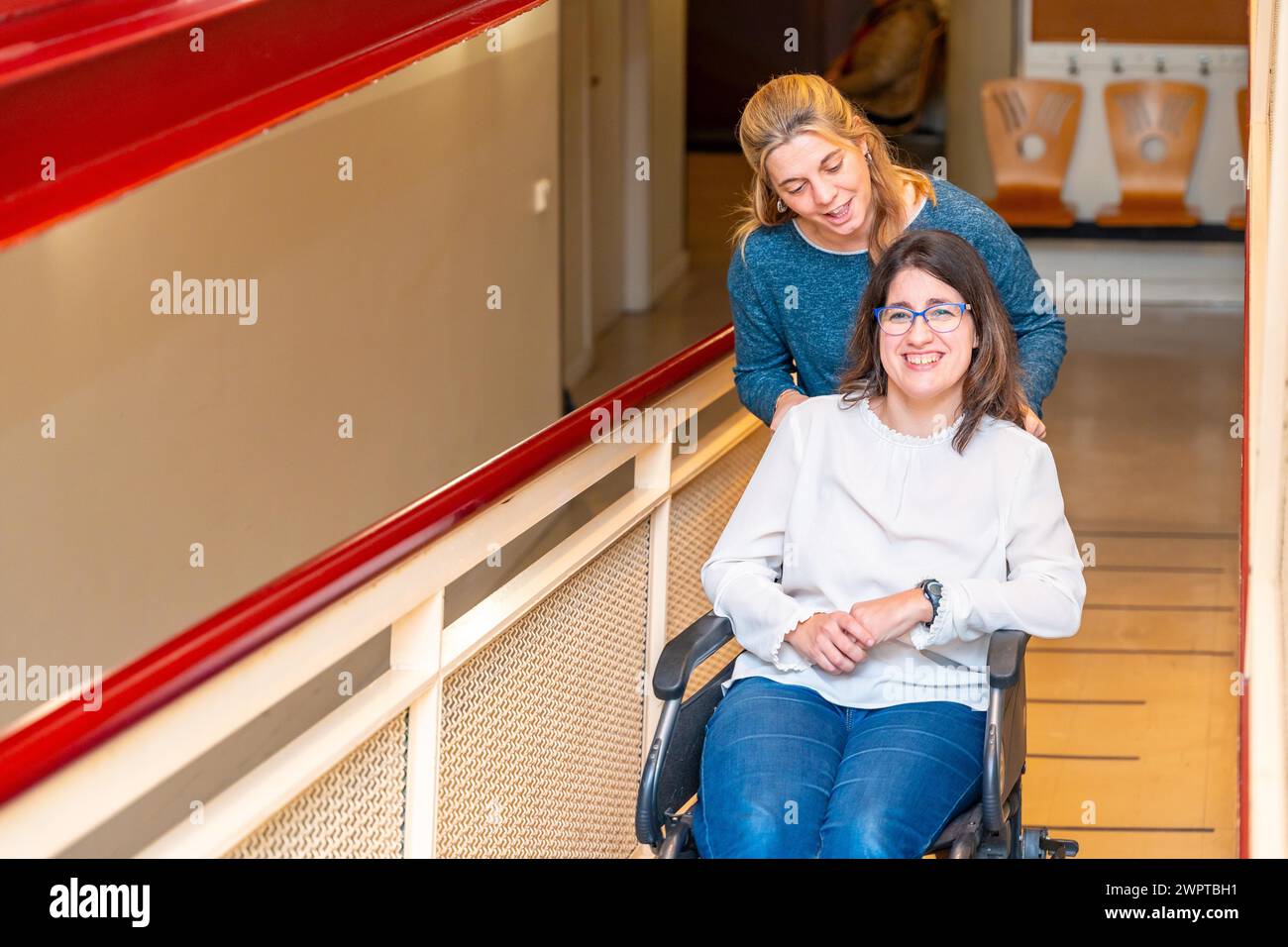 Woman walking a mental disabled woman in wheelchair along a day care ...
