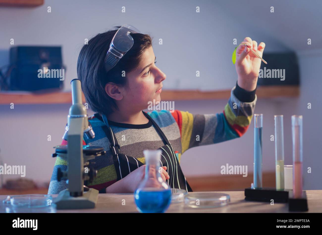 Cute young nerd in a home research laboratory wearing safety glasses is ...