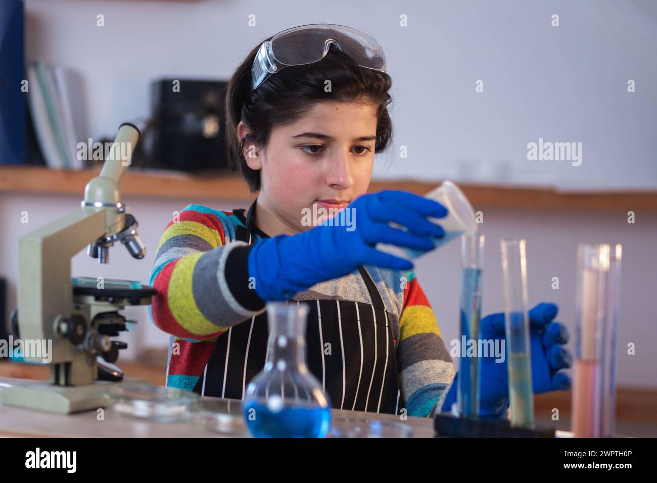 A funny Young Nerd in a home research laboratory wearing safety glasses and rubber gloves is ...