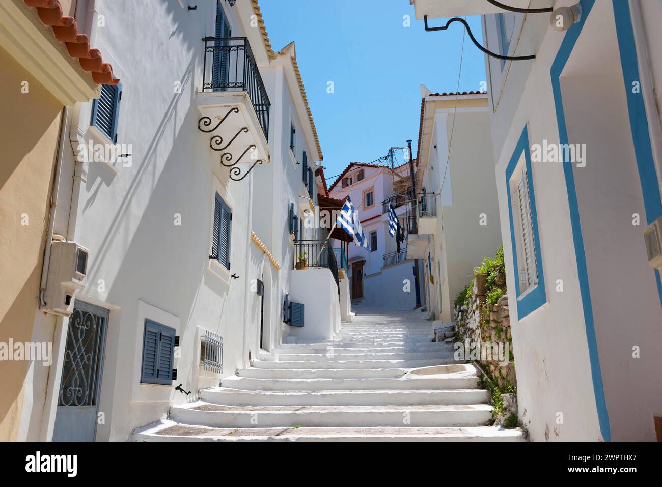 A sun-drenched alleyway with white houses and blue accents in Koroni ...