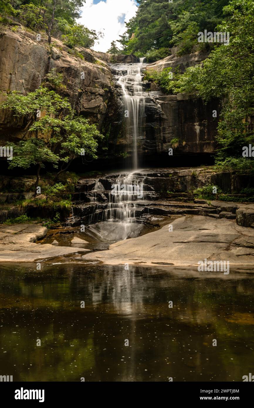 Gentle waterfall with its reflection visible in the clear, still water ...