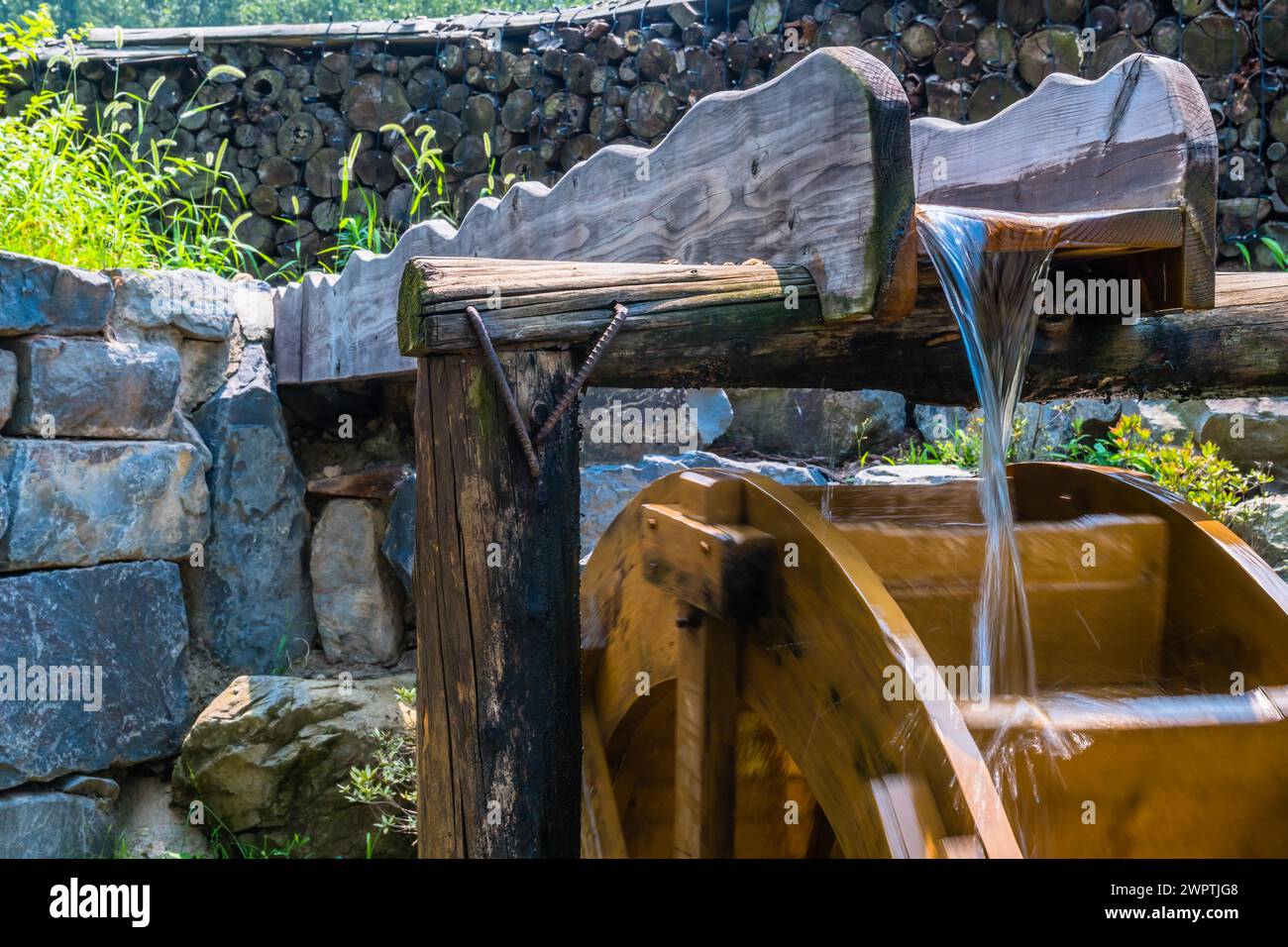 Water pouring onto a wooden water wheel by a stone wall, in South Korea ...