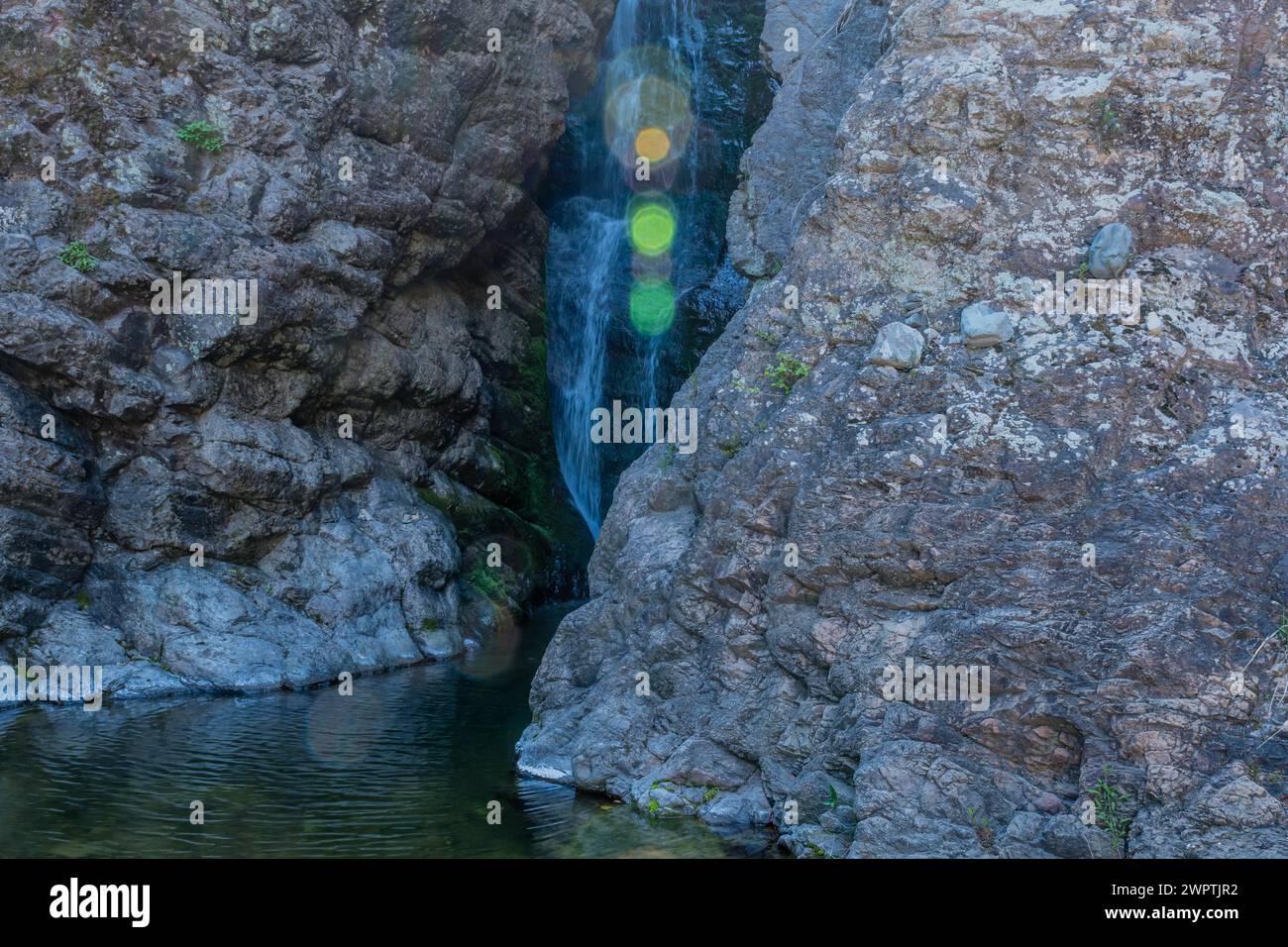 Serene waterfall cascading down rocky outcrop into a small pond, in ...