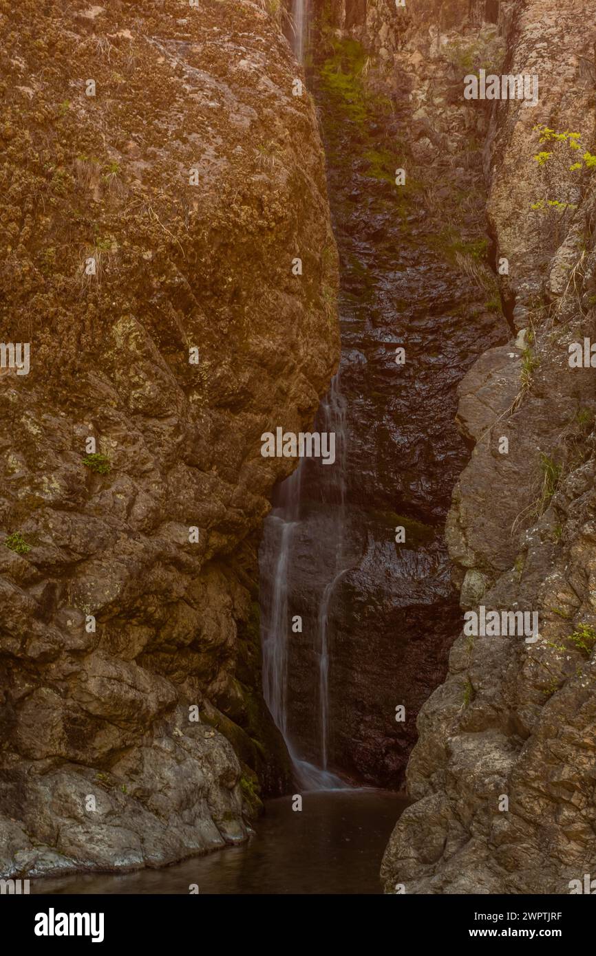 Vertical waterfall with sunlight casting shadows on the rocky walls, in ...