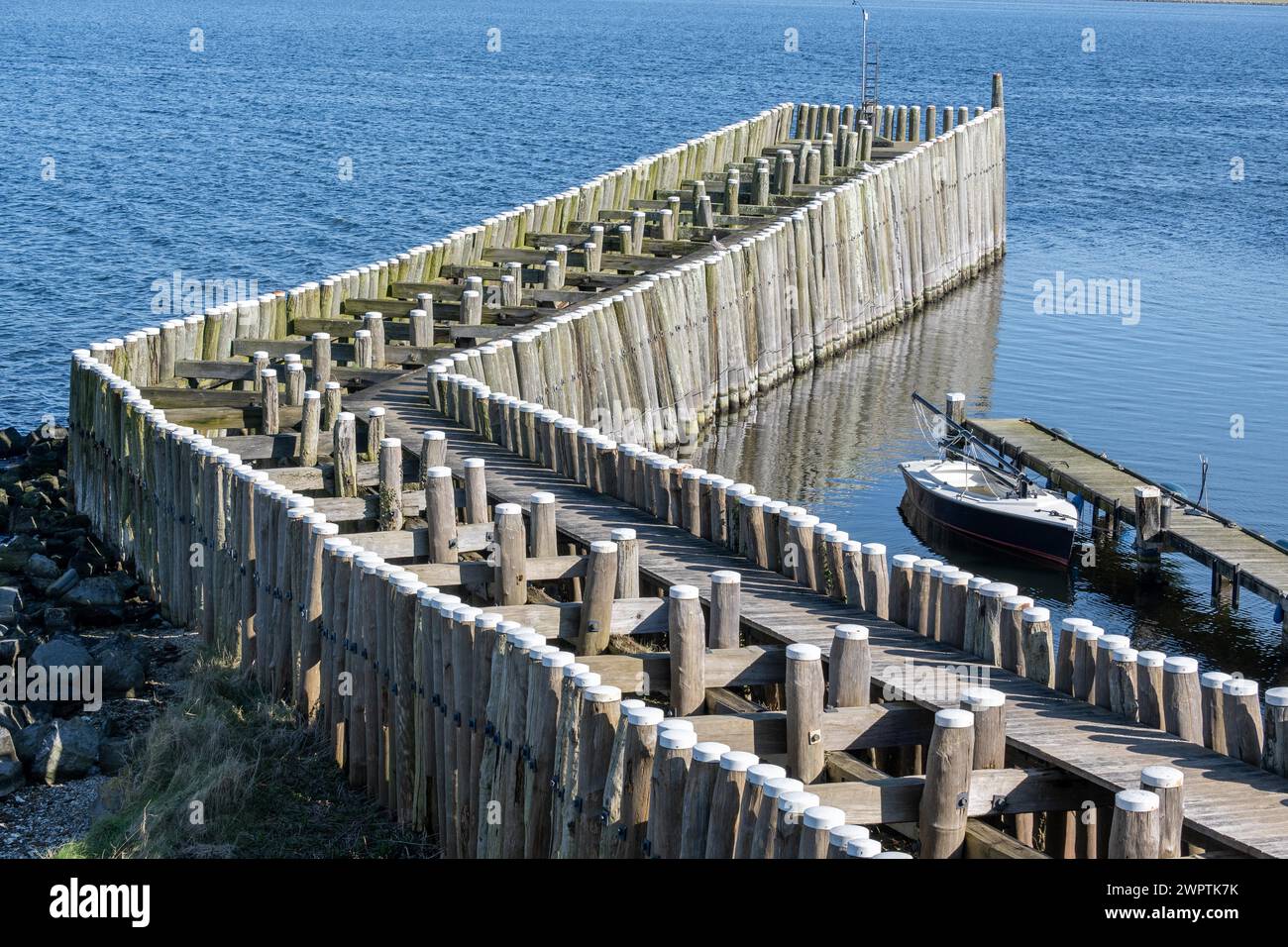 Wooden piles in the water form a jetty next to a boat at a quiet ...