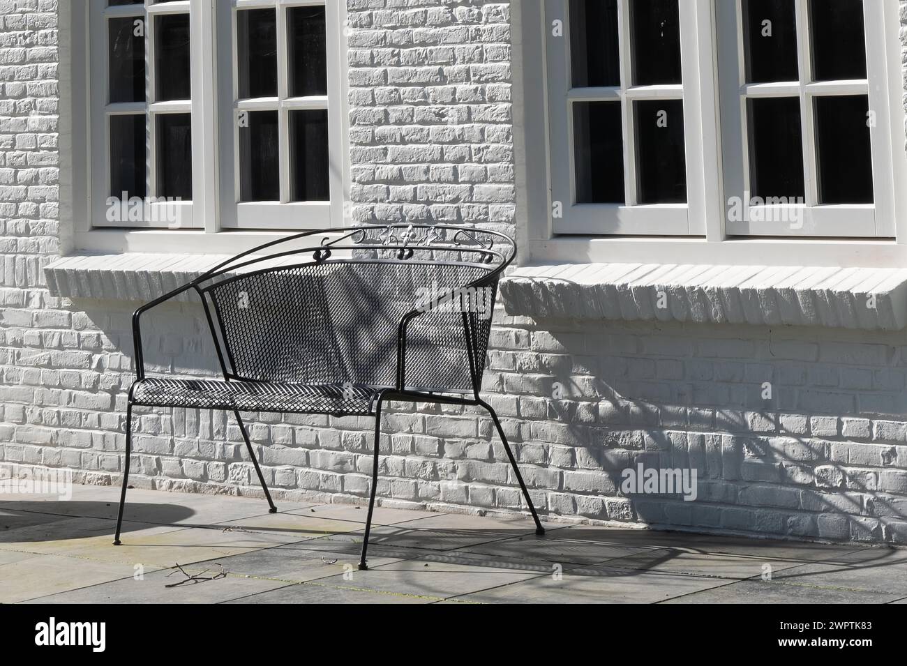 A black metal bench in front of a white wall casts a shadow in the ...
